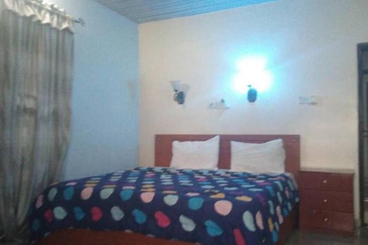 Quarto com cama, cortinas, luminária na parede e uma porta.