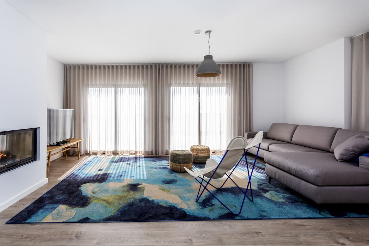 Uma sala de estar moderna com sofá, televisão, lareira e uma grande janela com cortinas.