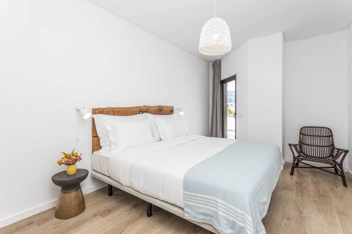 Quarto com cama, mesa de cabeceira, cadeira e luminária pendente.