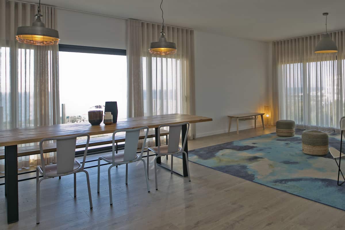 Uma sala de estar moderna com uma mesa de jantar de madeira, cadeiras brancas, um sofá e um tapete estampado.