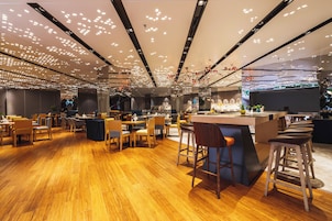 Interior moderno de restaurante com piso de madeira, várias áreas de estar e um balcão central.