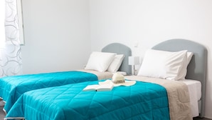 Quarto de hotel com duas camas, cada uma com colcha azul-esverdeada e almofadas brancas.