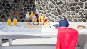 Montagem de piquenique com um muro de pedra ao fundo, incluindo uma mesa de madeira com comida, bebidas e um chapéu.