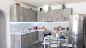 Uma cozinha moderna com armários cinzas, uma geladeira de aço inoxidável e uma área de refeições com mesa e cadeiras.