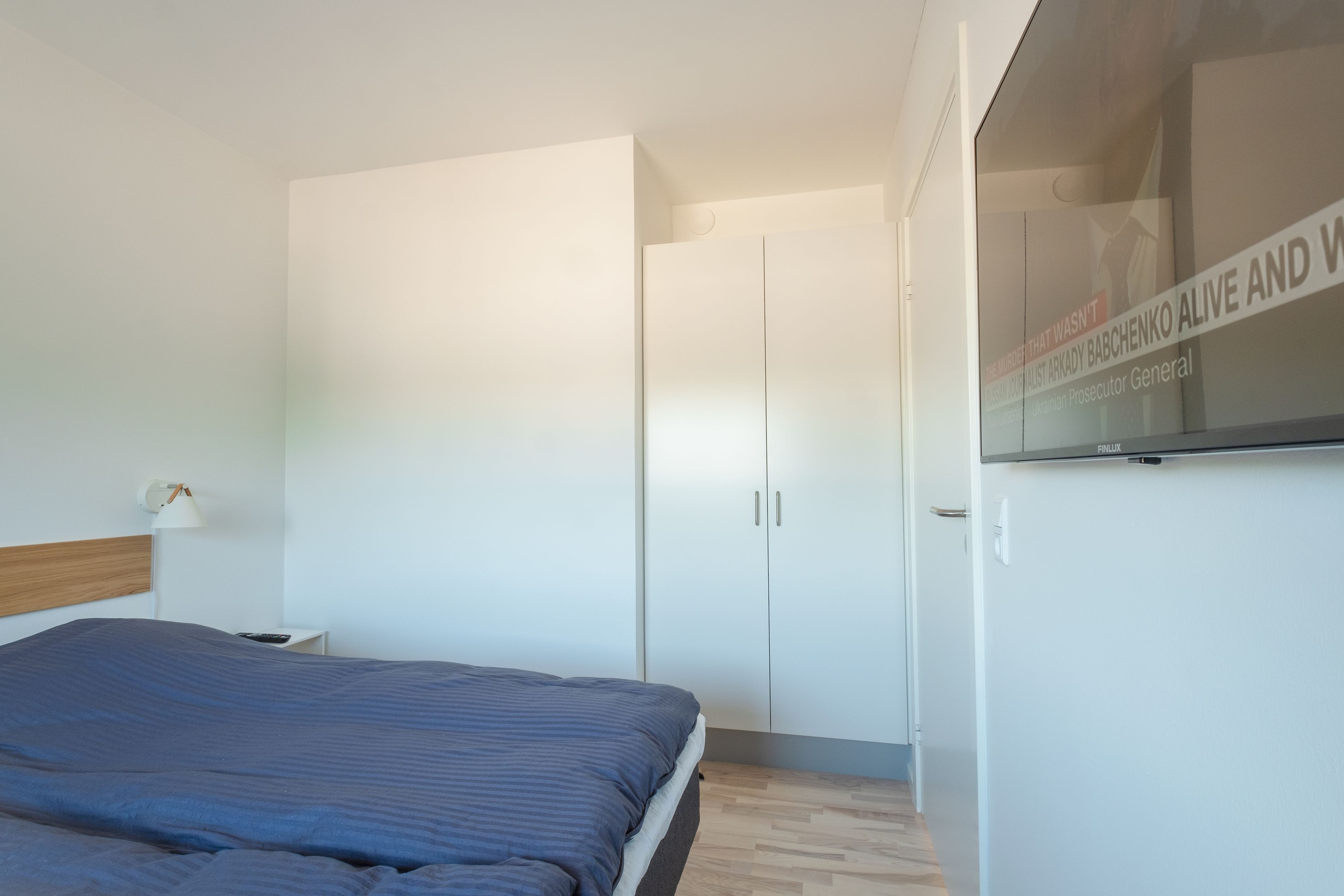 Quarto moderno com cama, mesa de cabeceira, guarda-roupa e parede de vidro com texto.
