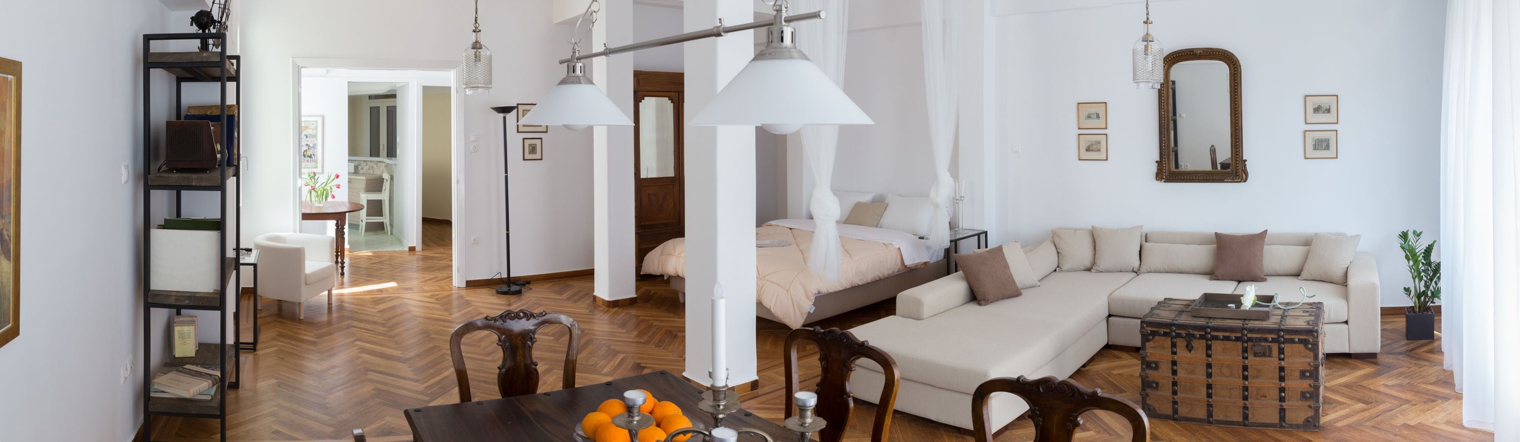 Uma sala de estar ampla com um conjunto de sofás, uma mesa de jantar de madeira com laranjas e um baú antigo.