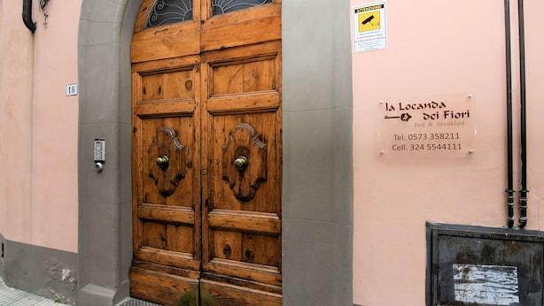Uma porta dupla de madeira com um arco de metal acima, um letreiro com informações de contato e o número '18' na parede.