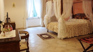 Quarto com cama de dossel, mesa de cabeceira de madeira, uma cadeira e janela com cortinas.