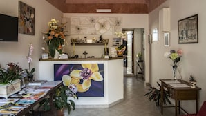 Uma área de recepção com balcão, uma pintura floral grande e várias plantas.
