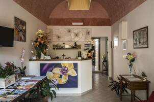 Uma área de recepção com balcão, uma pintura floral grande e várias plantas.