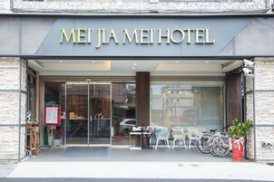 Entrada do Hotel Mei Jia Mei com fachada de vidro, uma placa e uma fileira de bicicletas na frente.