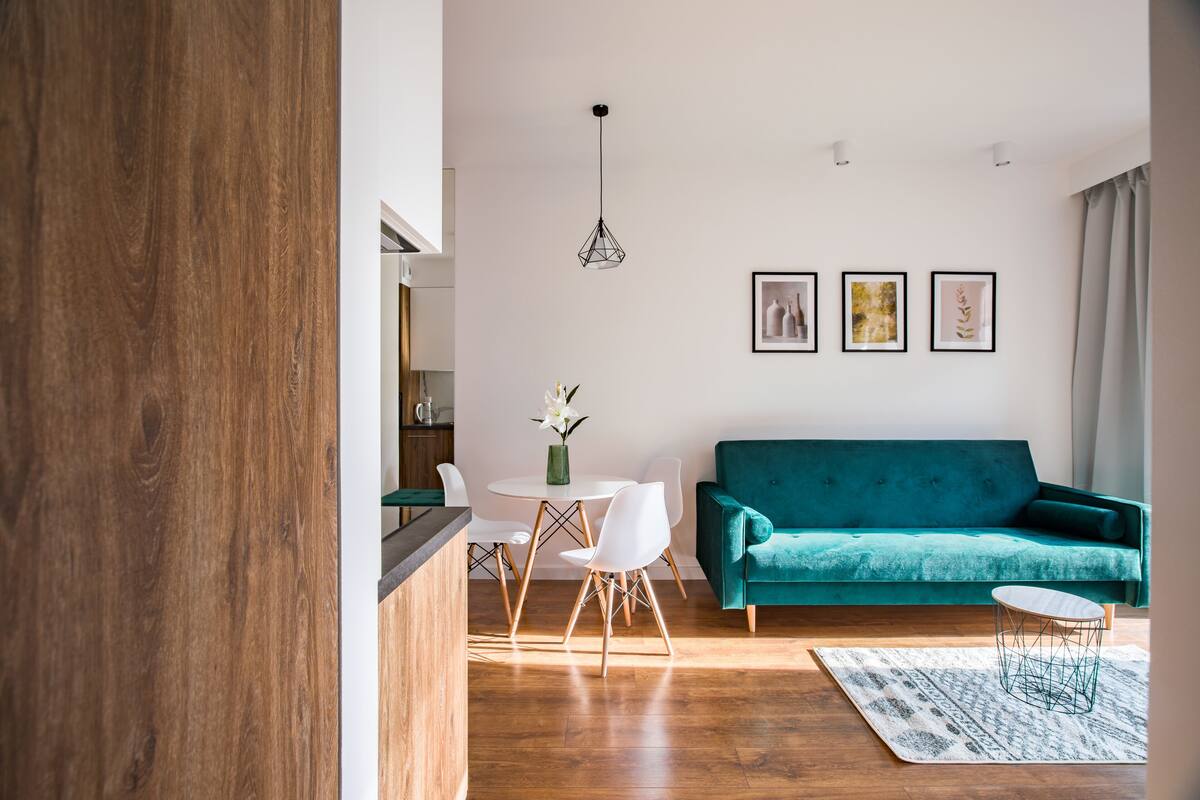 Uma sala de estar moderna com um sofá verde-água, cadeiras brancas, uma mesa de jantar com um vaso de flores e um lustre.