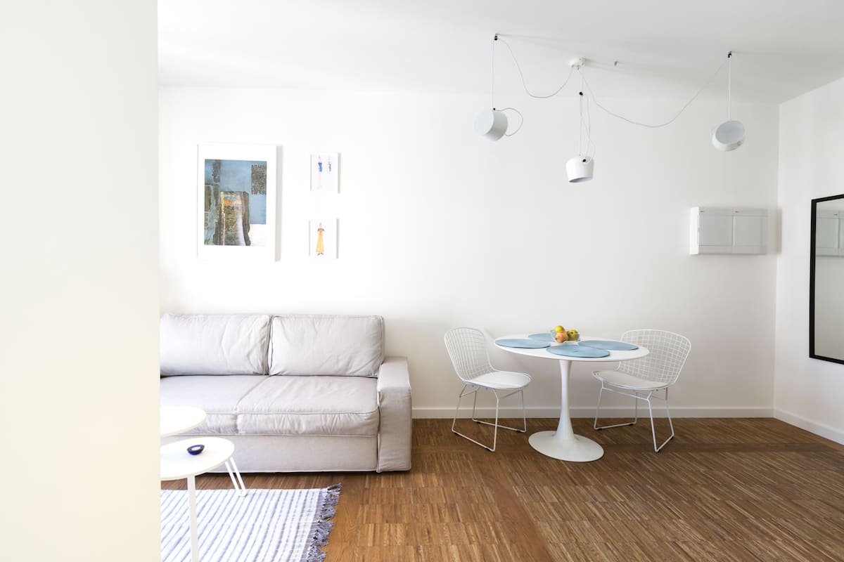 Uma sala de estar moderna com um sofá branco, uma mesa redonda com duas cadeiras e obras de arte na parede.