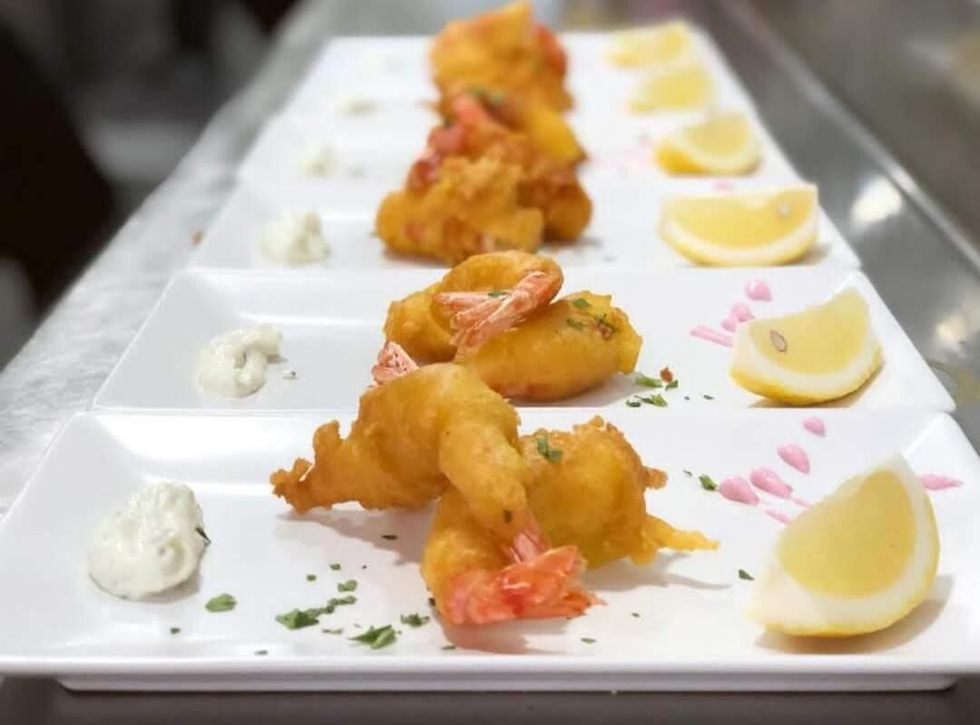 Um prato branco retangular com camarões fritos, rodelas de limão e molho cremoso.