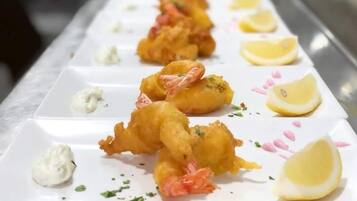 Um prato branco retangular com camarões fritos, rodelas de limão e molho cremoso.