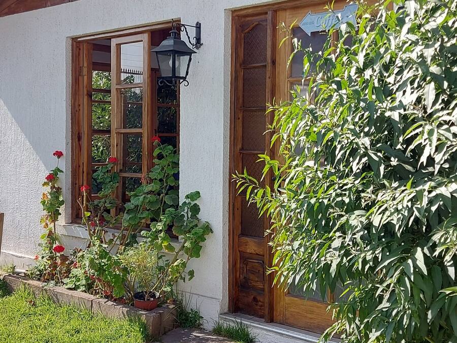Um edifício de madeira com telhado inclinado, porta de madeira e uma janela. Há um jardim com grama e plantas em frente ao edifício.