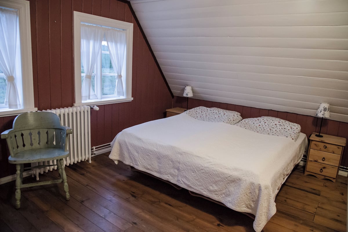 Quarto com uma cama grande, duas mesas de cabeceira, uma cadeira e um radiador.