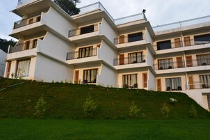 Um edifício com vários andares, varandas, telhado inclinado e uma colina gramada em primeiro plano.
