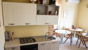 Uma cozinha compacta com fogão a gás, lava-louças e uma pequena área de refeições com mesa redonda e cadeiras.