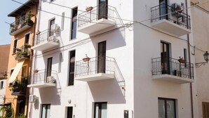 Um edifício com vários andares, varandas, telhado plano e uma rua em frente.