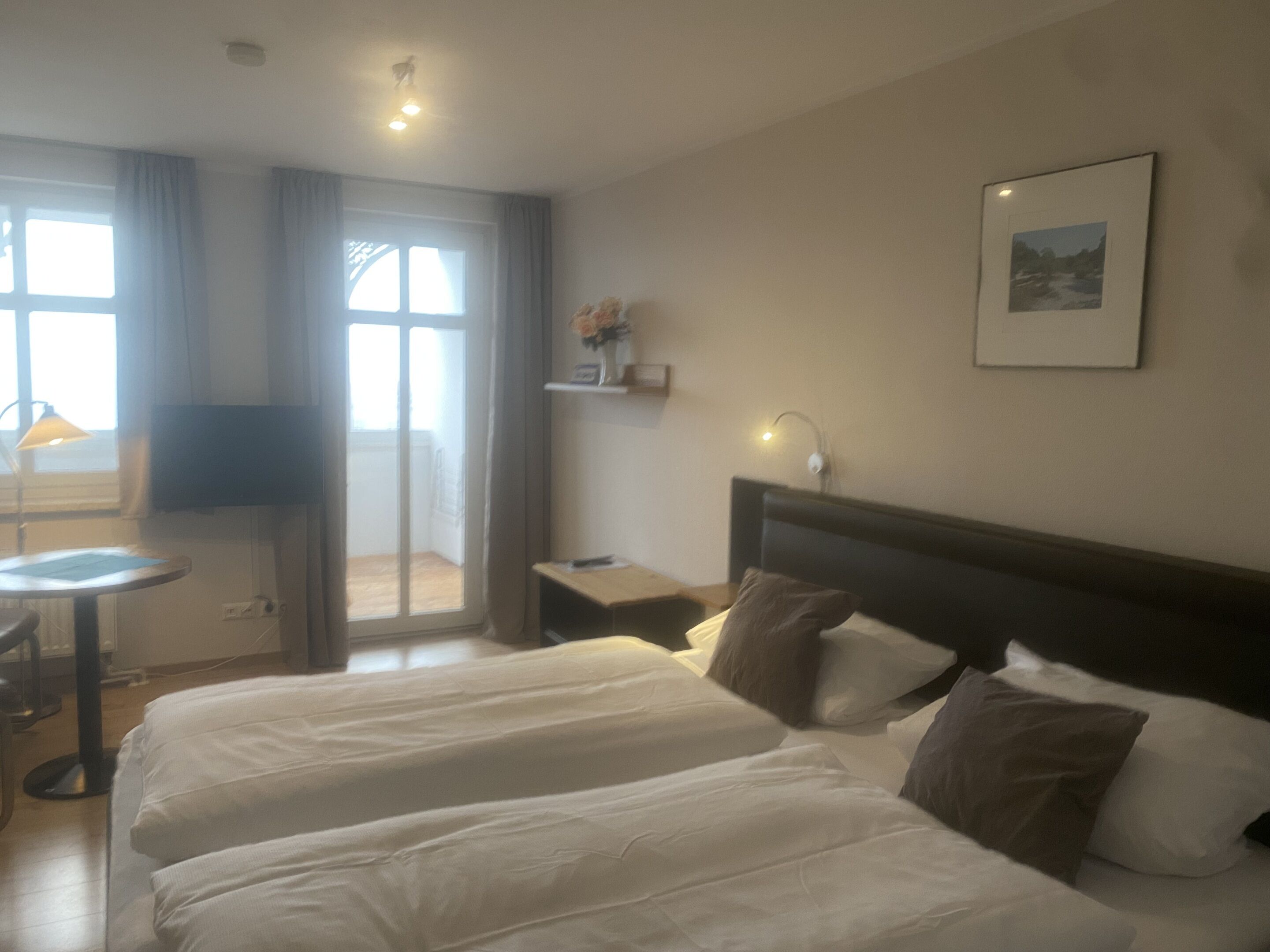 Quarto de hotel com cama, escrivaninha, cadeira, abajur e um quadro na parede.