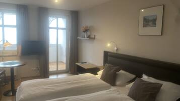 Quarto de hotel com cama, escrivaninha, cadeira, abajur e um quadro na parede.