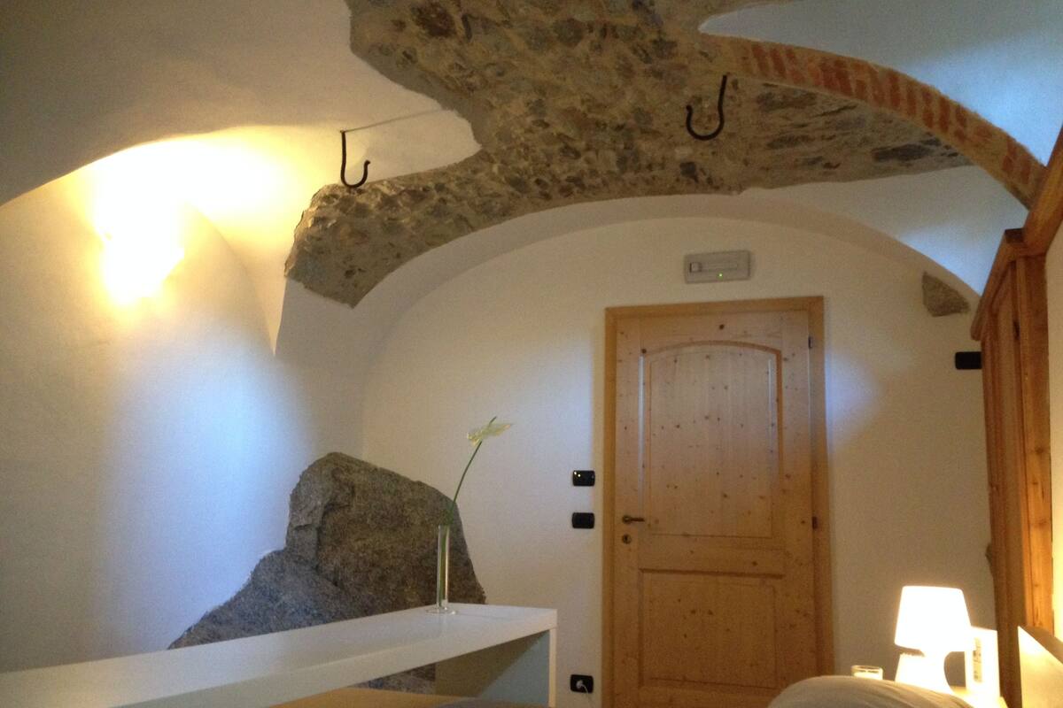 Um quarto com teto de pedra, porta de madeira, prateleira branca e um abajur.
