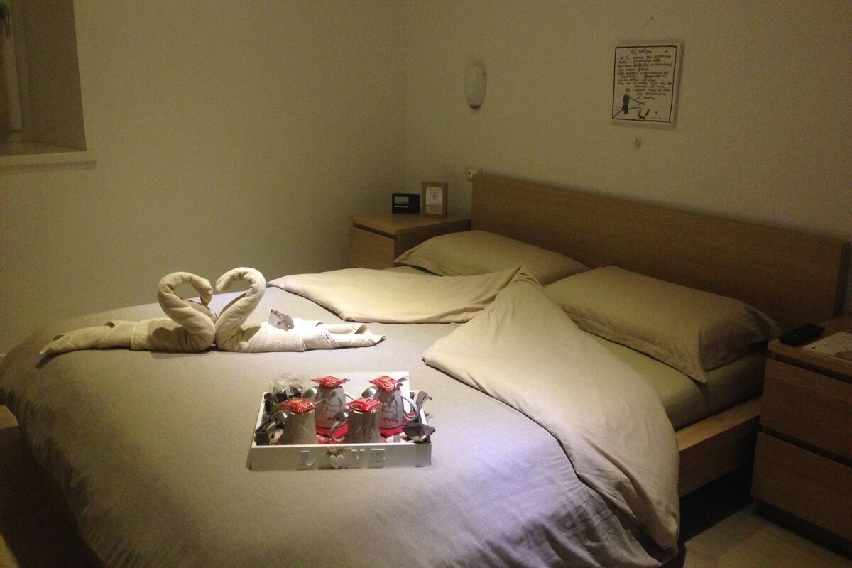 Cama bem arrumada com toalha em formato de cisne e bandeja de chocolates.