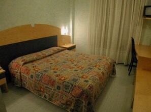 Quarto de hotel com cama, mesa de cabeceira, escrivaninha e cadeira.