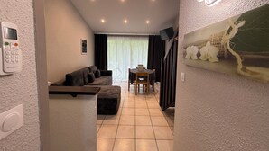 Uma sala de estar moderna com sofá, mesa de jantar e cadeiras, teto com iluminação embutida e um quadro na parede.