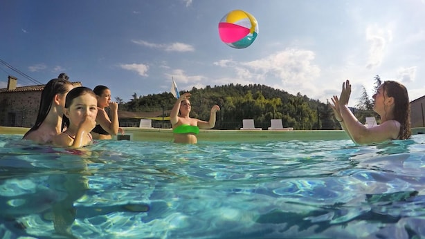Piscina com água cristalina, uma boia e pessoas brincando.