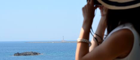 Uma pessoa fotografando um farol à beira-mar.
