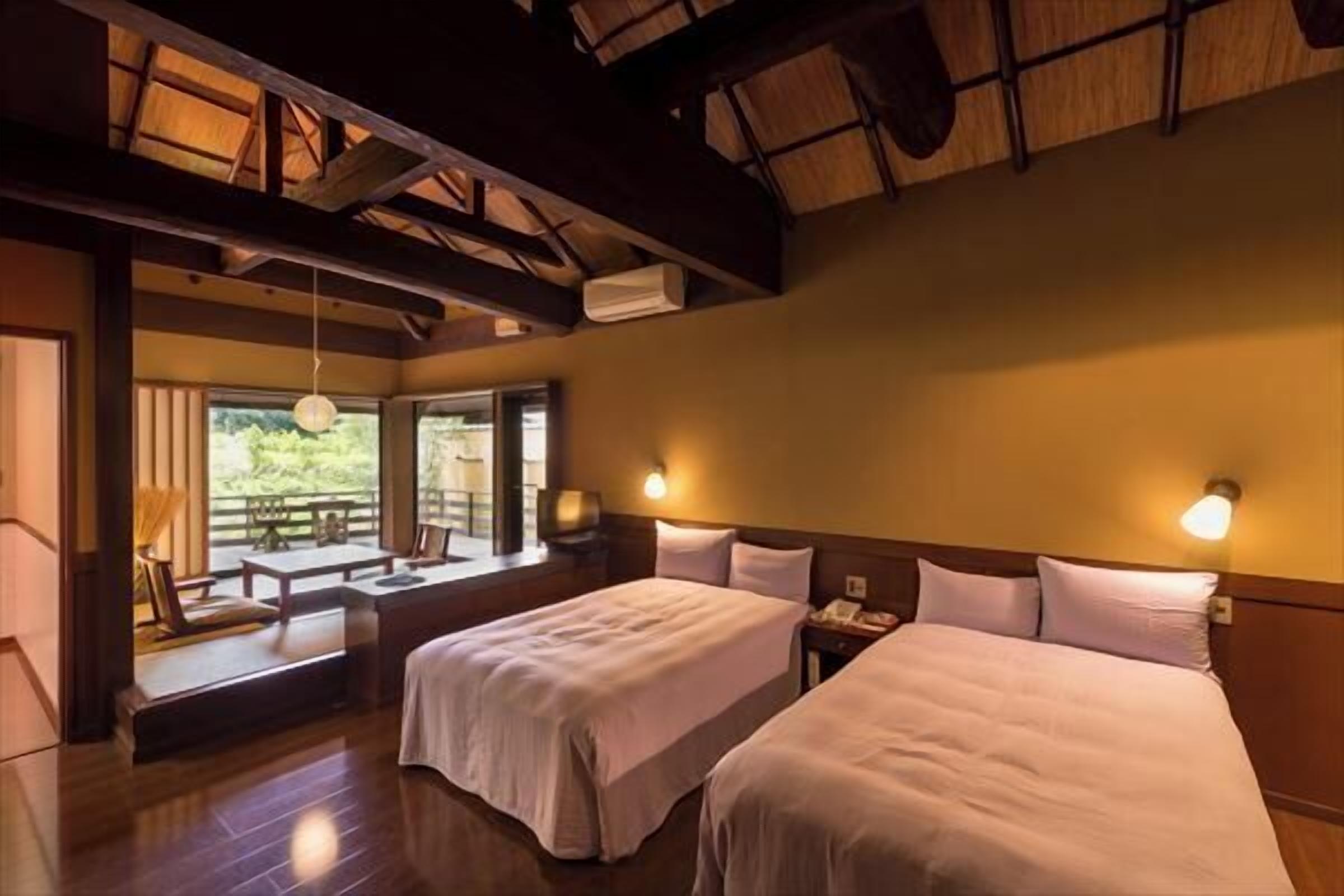 Quarto de hotel com duas camas, teto de madeira, janela com vista e mesa com cadeiras.