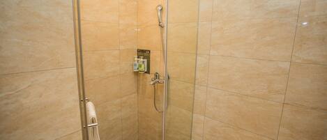 Um chuveiro com divisória de vidro, azulejos bege, um porta-toalhas e um dispensador de sabonete na parede.