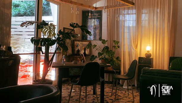Quarto com teto de madeira, mesa de jantar com cadeiras, sofá e várias plantas em vasos.