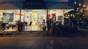 Um hotel chamado HOTEL NIZZA com entrada visível, área de estar externa e plantas em vasos.