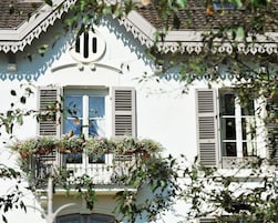 Um edifício branco com varanda, persianas e grades decorativas na janela.
