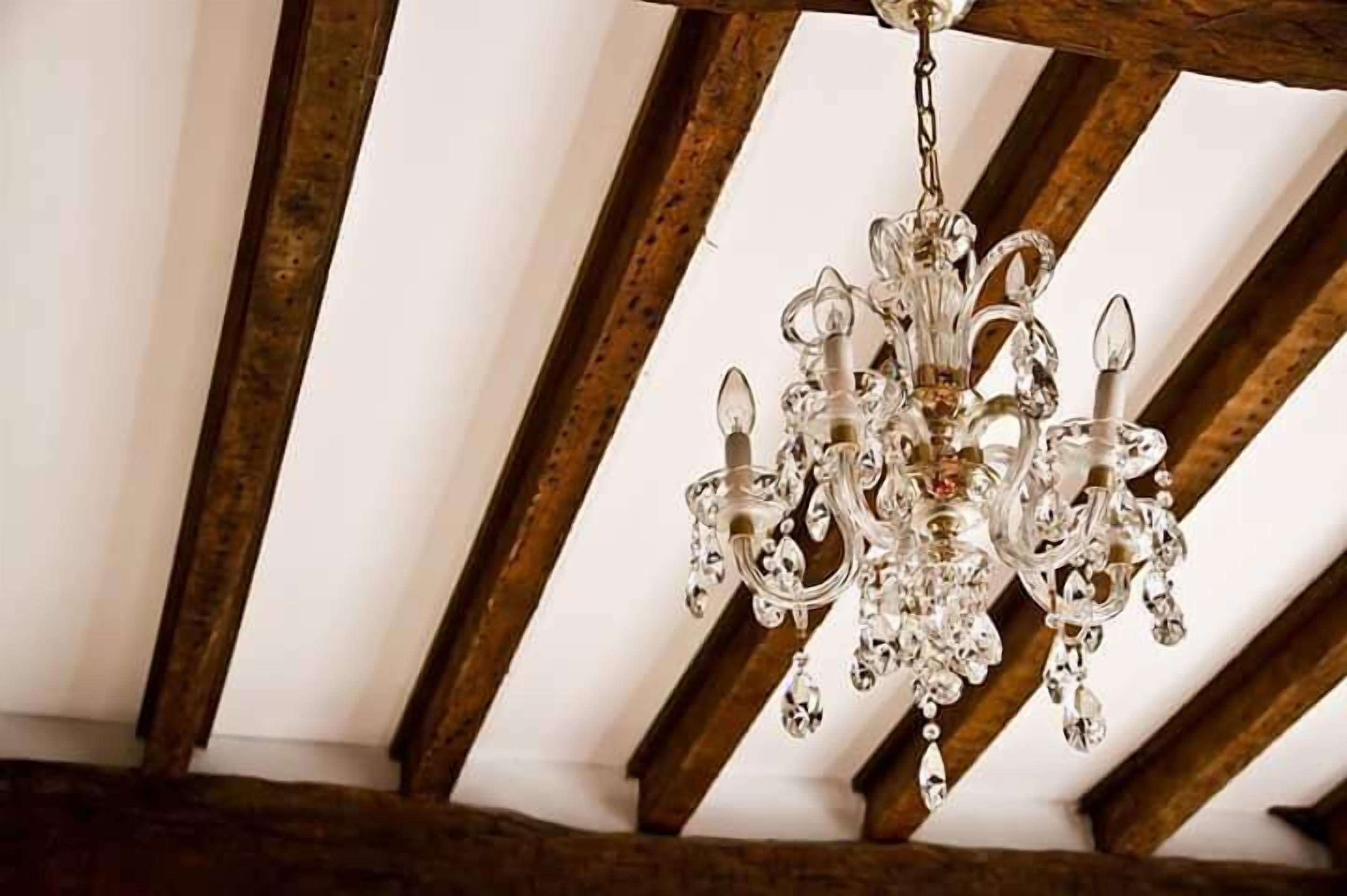 Um candelabro com vários braços e detalhes em cristal pendurado em uma estrutura de vigas de madeira.