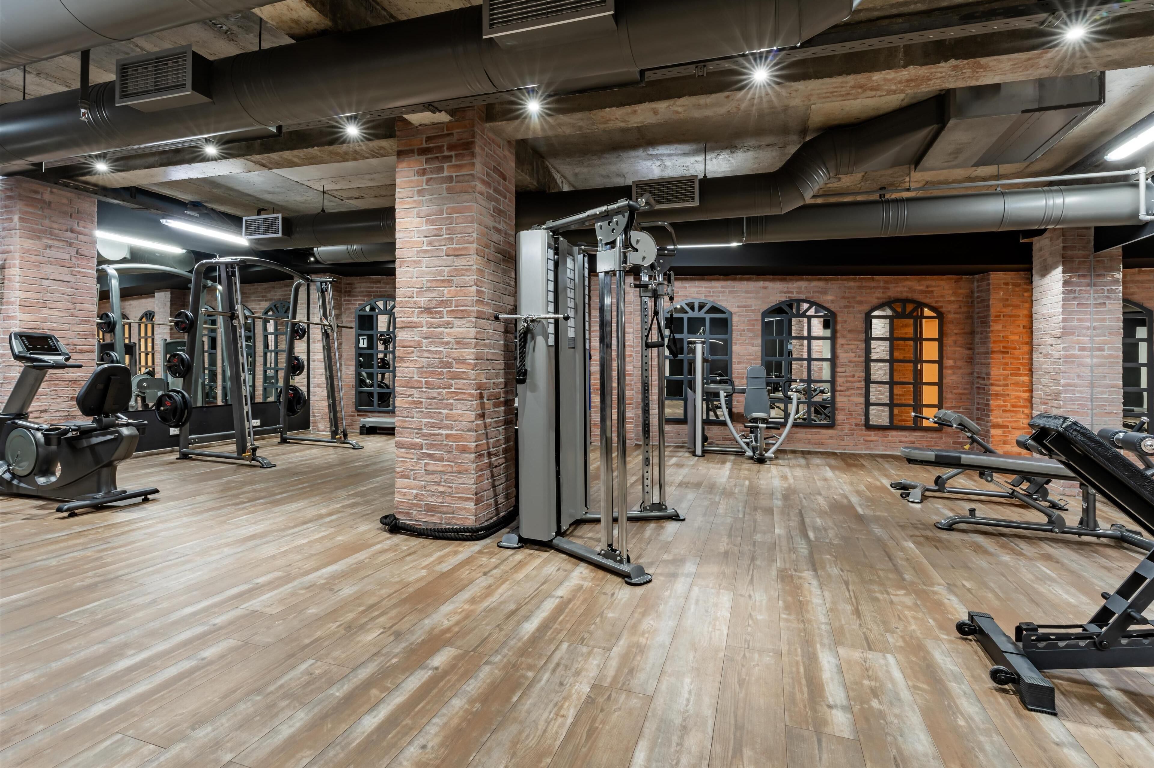Uma academia com paredes de tijolo, piso de madeira e diversos equipamentos de ginástica.