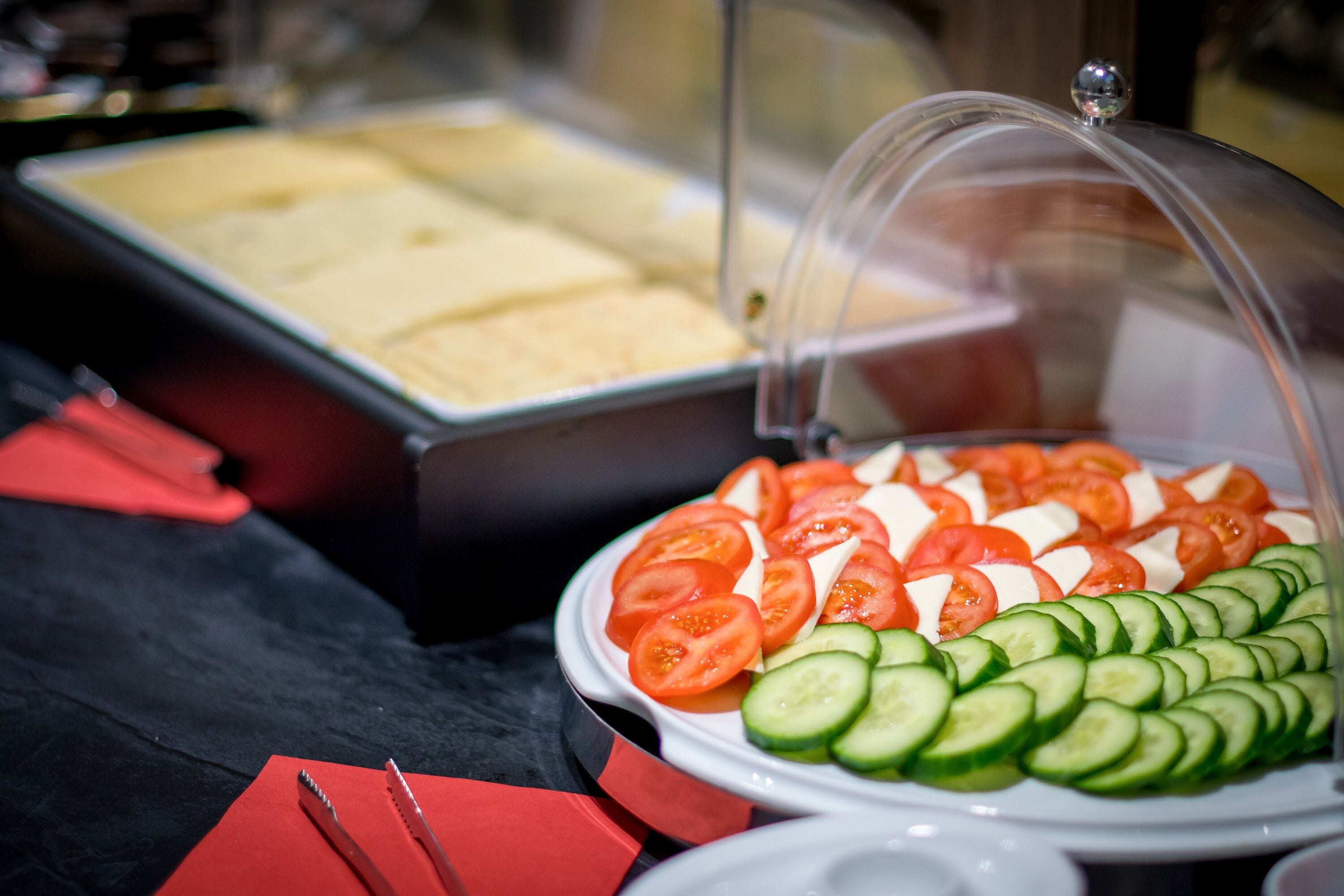 Buffet com variedade de alimentos, incluindo tomates fatiados, pepinos e queijo.