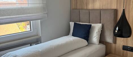 Quarto moderno com cama, mesa de cabeceira e janela com persianas.