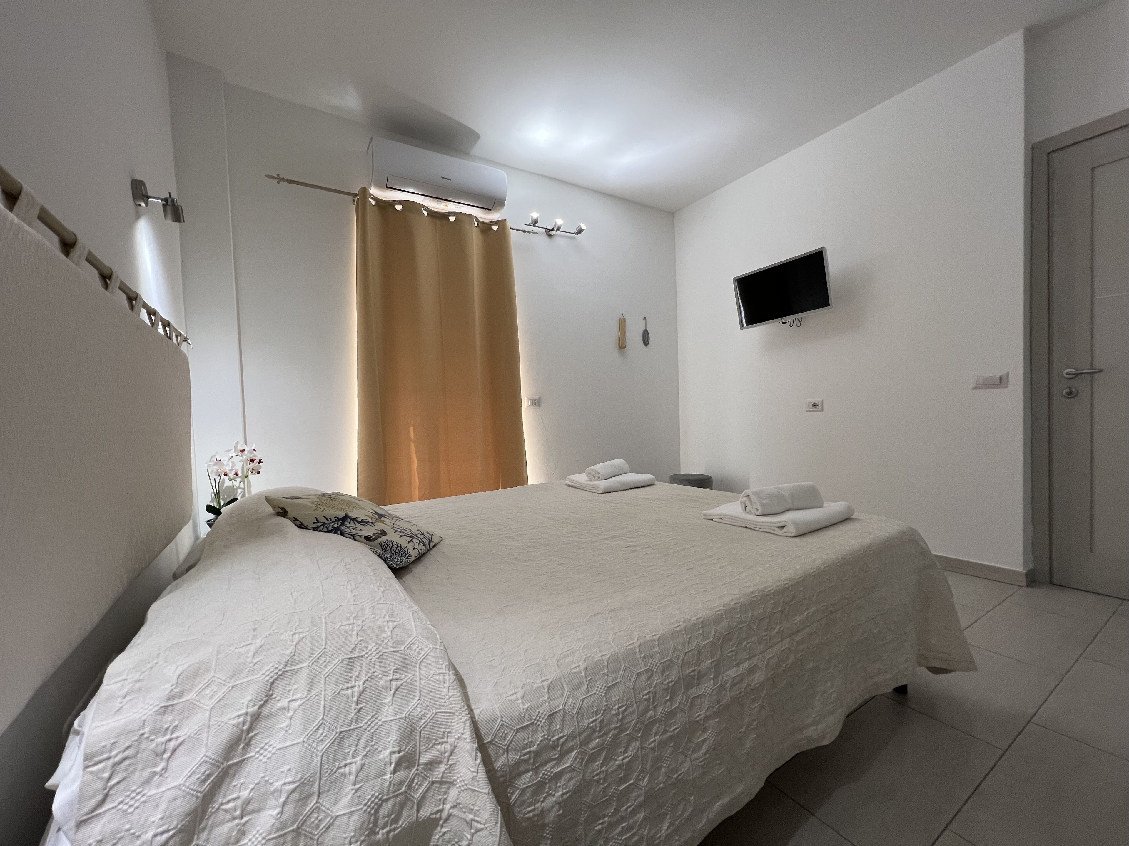 Quarto de hotel com uma cama, televisão de tela plana na parede, banheiro com cortina de chuveiro e uma porta.