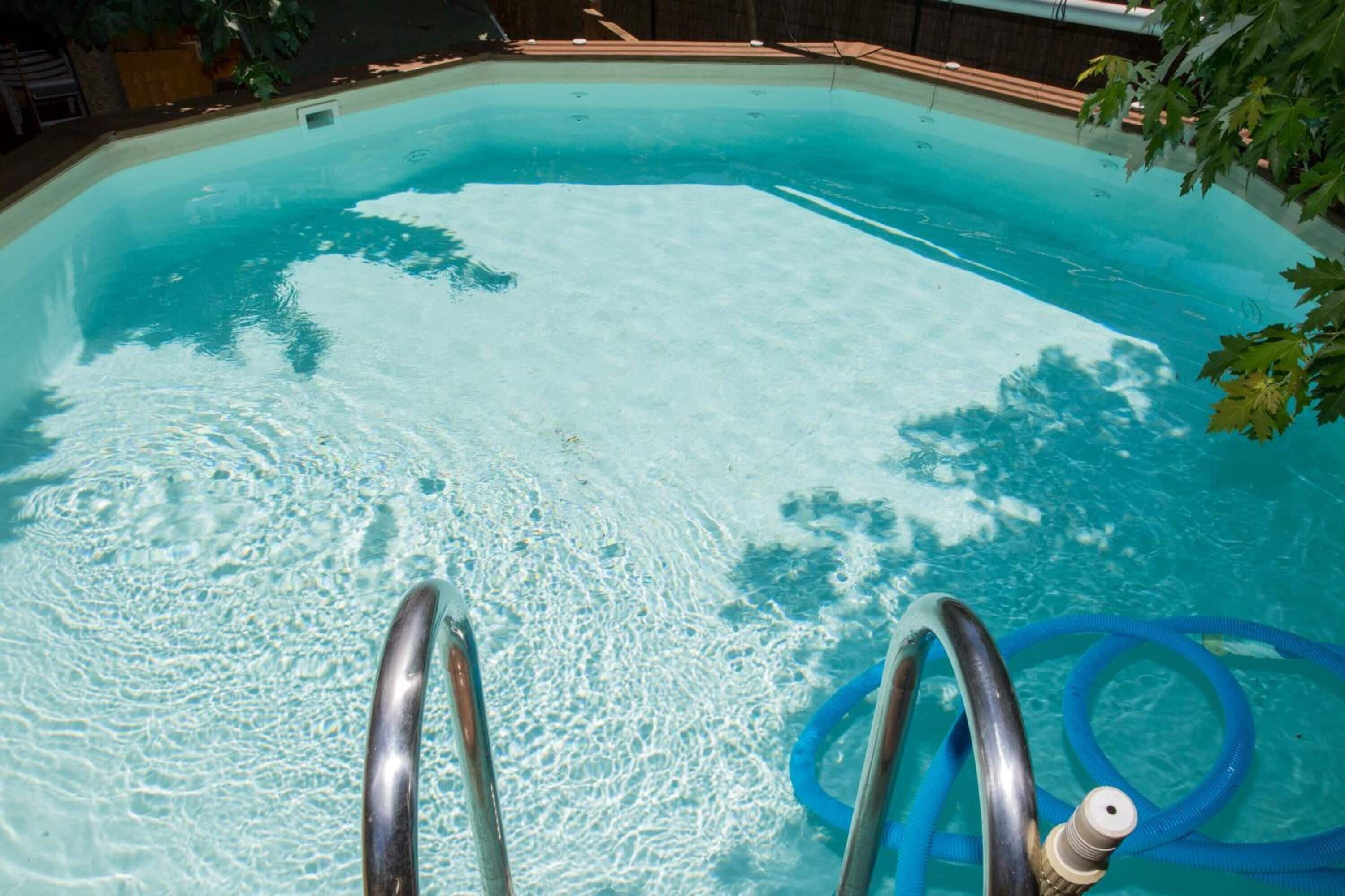 Uma piscina límpida com escadas de metal e uma mangueira azul.