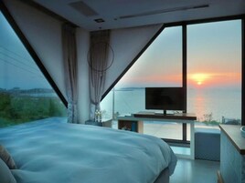 Quarto moderno com uma cama grande, televisão e vista do pôr do sol sobre a água.