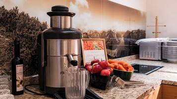 Uma bancada de cozinha com uma cafeteira, um frasco de azeite, uma tigela de maçãs e uma fotografia de vegetais.