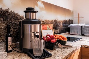 Uma bancada de cozinha com uma cafeteira, um frasco de azeite, uma tigela de maçãs e uma fotografia de vegetais.