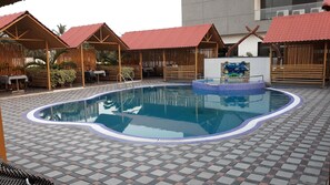 Piscina com deck ladrilhado, cercada por estruturas de madeira com telhados vermelhos, e um mural retratando a vida aquática.