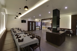 Um restaurante moderno com várias mesas de jantar, uma ilha central e iluminação pendente.