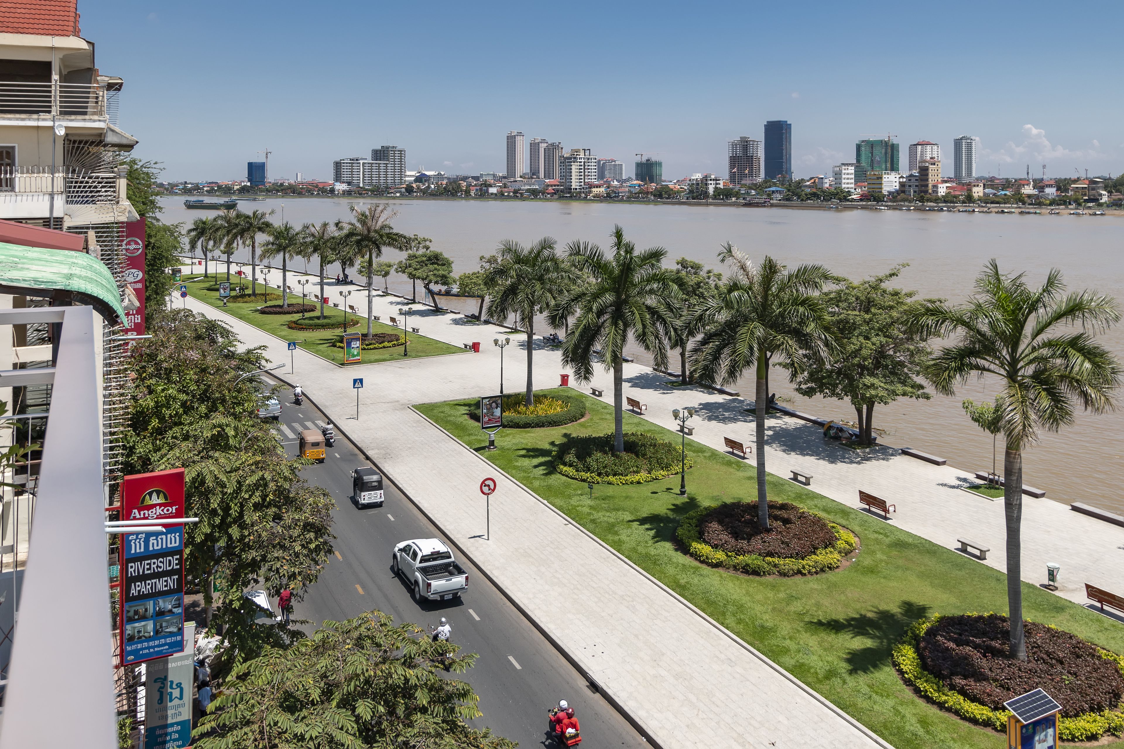 Vista ribeirinha com uma estrada, palmeiras e o horizonte da cidade ao fundo.
