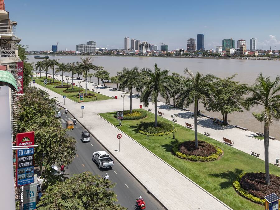 Vista ribeirinha com uma estrada, palmeiras e o horizonte da cidade ao fundo.